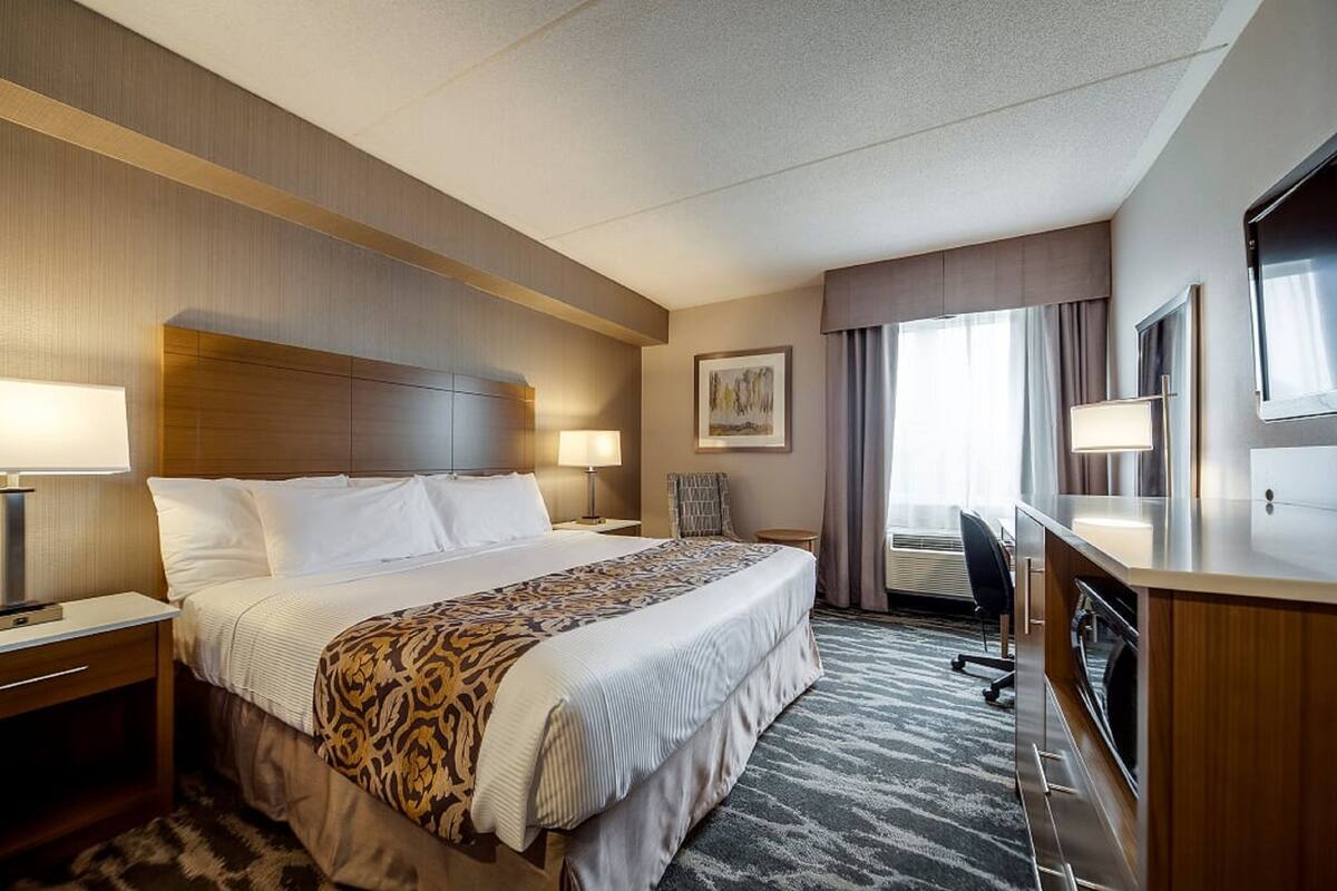 Quarto de hotel com uma cama grande, escrivaninha, cadeira, televisão e janela com cortinas.