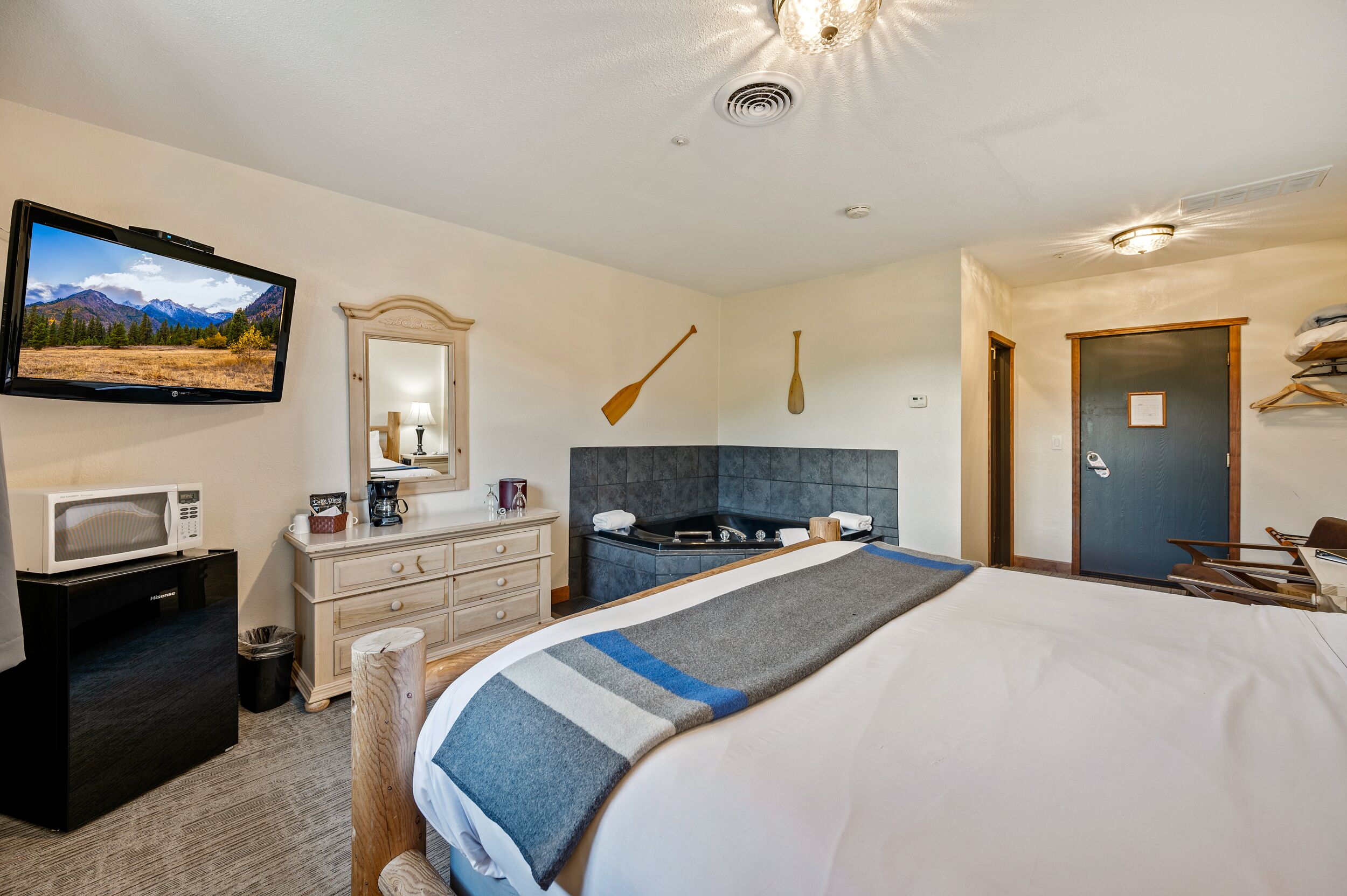 Quarto de hotel com cama, televisão, micro-ondas, escrivaninha, cadeira, banheira e porta.