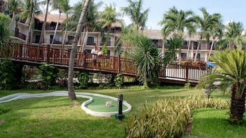Um resort com piscina, palmeiras e uma ponte ligando os edifícios.