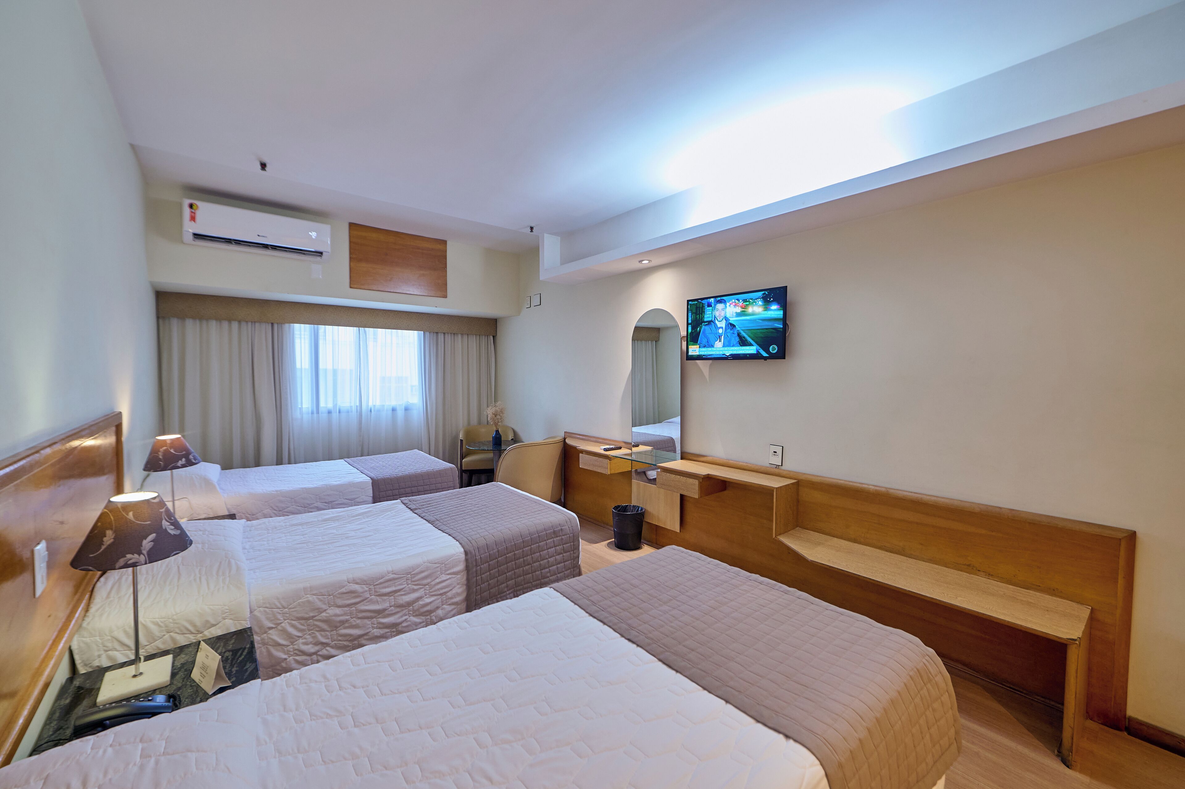 Quarto de hotel com duas camas, televisão, escrivaninha e espelho.