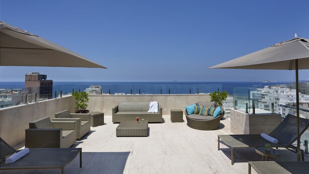 Terraço no telhado com área de estar externa, incluindo sofás e cadeiras, e vista para o oceano.