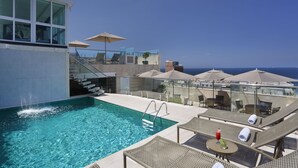 Uma área de piscina no terraço, com água azul cristalina, espreguiçadeiras e guarda-sóis.