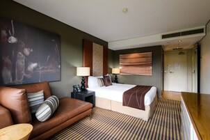 Quarto de hotel com cama, sofá, mesa de centro e uma grande pintura abstrata na parede.
