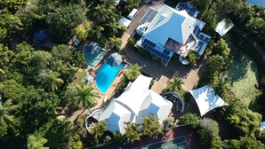 Vista aérea de uma propriedade residencial com piscina, painéis solares e uma casa grande e branca.