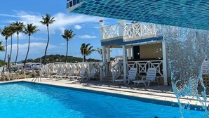 Uma área de piscina com água azul cristalina, cadeiras de espreguiçadeira brancas e um elemento aquático.