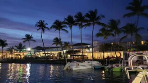 Um hotel à beira-mar com piscina, palmeiras e um barco atracado nas proximidades.