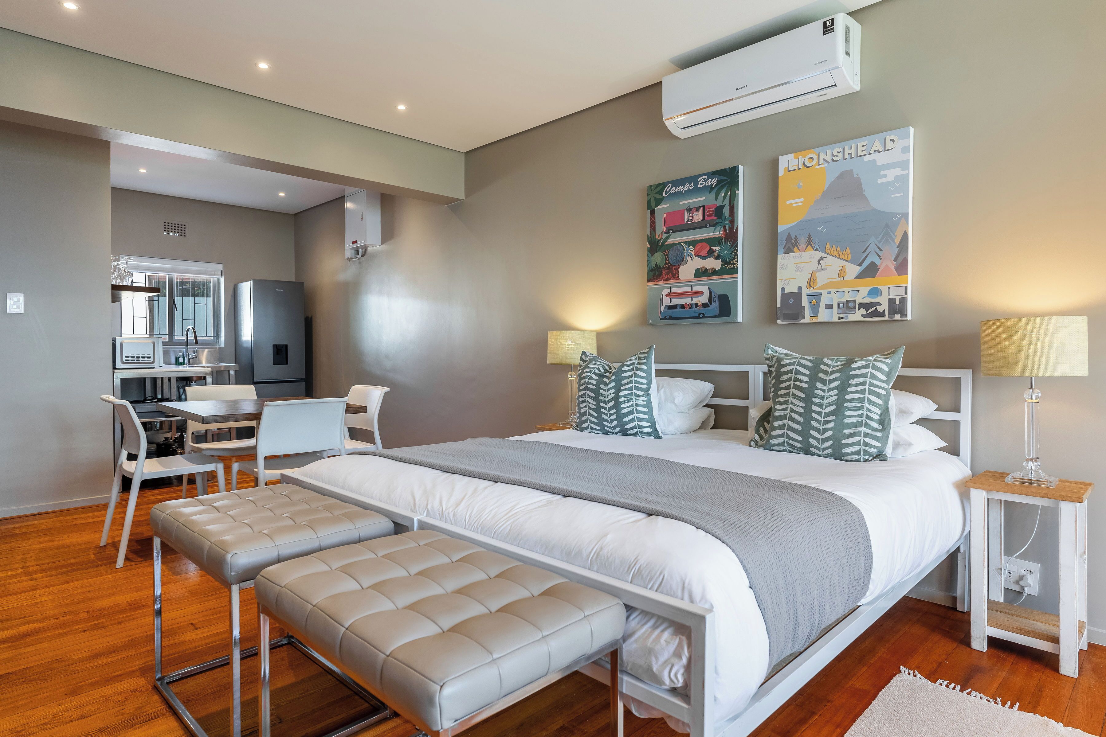 Quarto moderno com uma cama grande, mesas de cabeceira, um banquinho e uma área de trabalho com cadeiras.