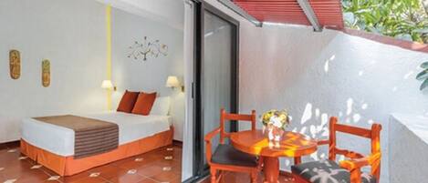 Quarto de hotel com cama, mesa e cadeiras, e vista para o verde lá fora.