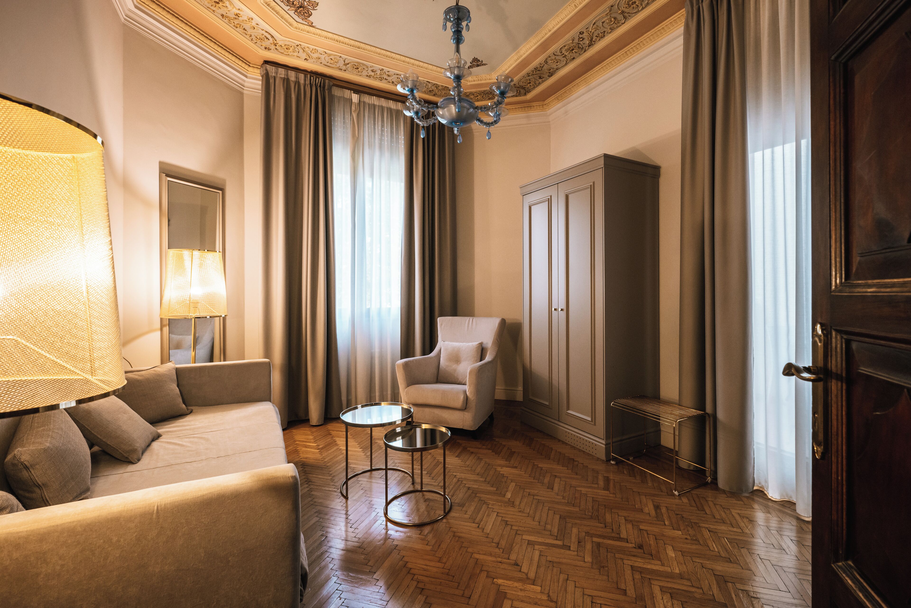 Quarto com sofá, poltrona, mesinhas redondas, um candeeiro e um guarda-roupa.