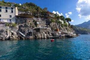 Um edifício costeiro com várias varandas, uma escadaria que leva aos andares superiores e vista para o mar.