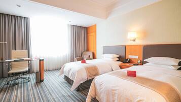 Quarto de hotel com duas camas, uma escrivaninha, uma cadeira e um abajur.