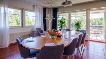 Uma sala de conferências com uma mesa grande, cadeiras, um projetor e vista para o exterior.