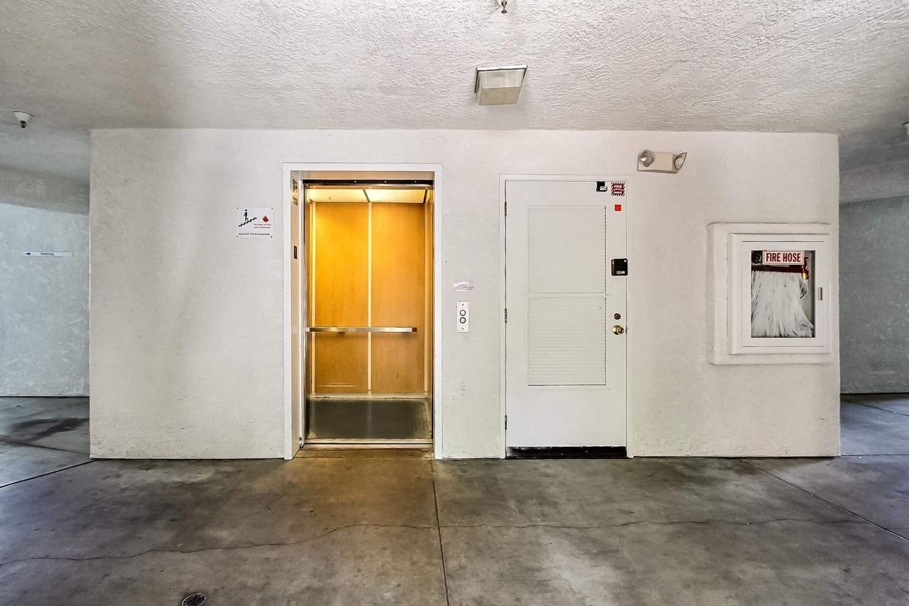 Um elevador em um corredor com uma porta de mangueira de incêndio e uma placa indicando um armário de mangueira contra incêndio.