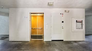 Um elevador em um corredor com uma porta de mangueira de incêndio e uma placa indicando um armário de mangueira contra incêndio.