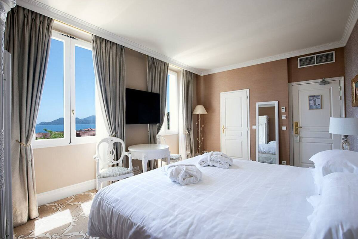 Quarto de hotel com uma cama grande, televisão, secretária e uma cadeira.