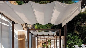 Uma área de estar ao ar livre banhada pelo sol, com assentos acolchoados brancos e uma estrutura de pérgola de madeira.