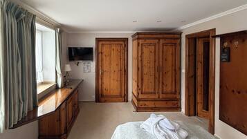 Quarto com cama, guarda-roupa de madeira, televisão e janela com cortinas.