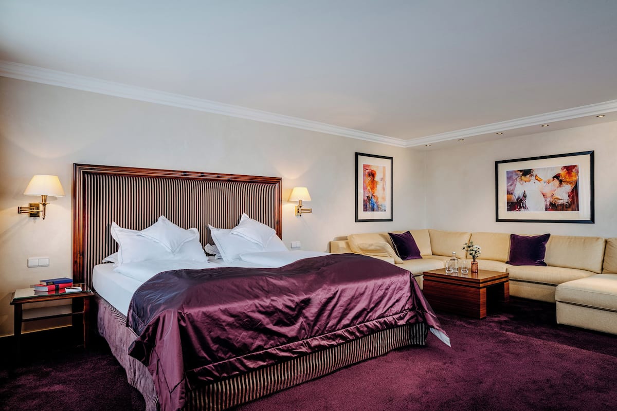 Quarto de hotel com uma cama grande, um sofá, uma mesa de centro e duas luminárias fixadas na parede.