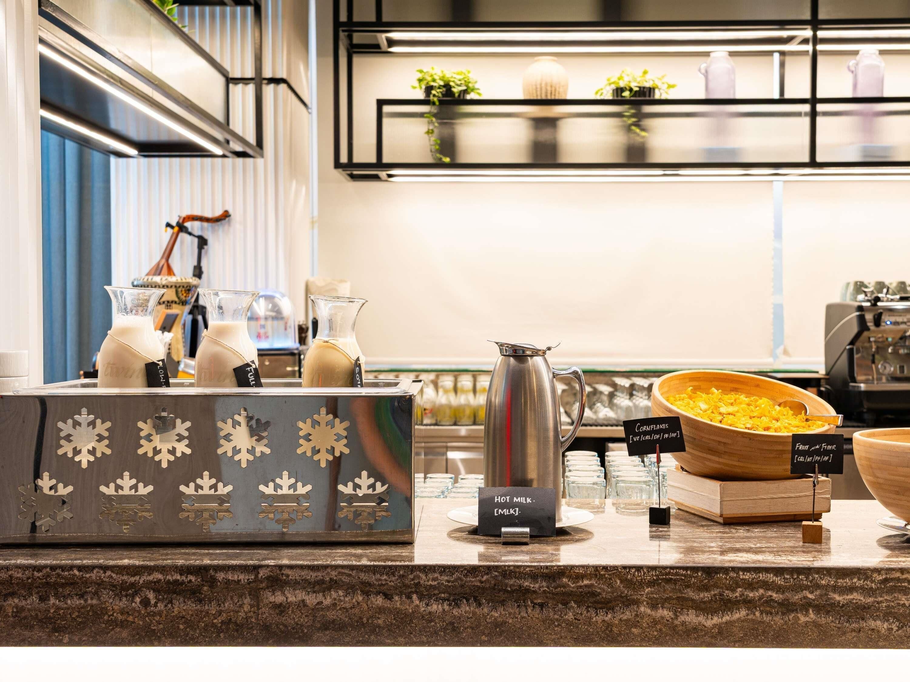 Uma estação de café com dosadores de leite, um dosador para leite quente, e recipientes com flocos de milho e fruta.