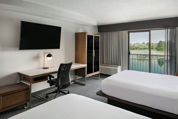Quarto de hotel com escrivaninha, cadeira, televisão, guarda-roupa e cama.