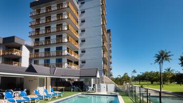 Um hotel com vários andares, área de piscina, mobiliário de exterior e um jardim cercado.