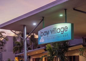 Placa para 'Bay Village Tropical Retreat' com um edifício moderno e palmeiras ao fundo.
