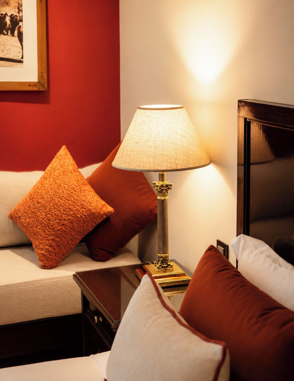 Quarto de hotel com uma cama, uma mesa de cabeceira com abajur e um quadro pendurado na parede.