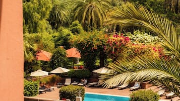 Área de piscina de hotel com espreguiçadeiras e guarda-sóis, rodeada por vegetação exuberante e um céu azul límpido.