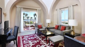 Quarto de hotel com varanda, um sofá, uma mesa de centro e uma televisão.