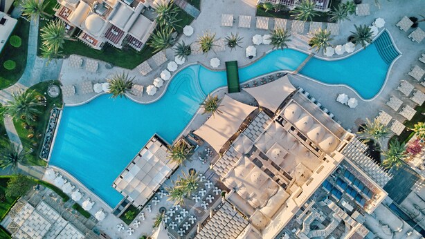 Vista aérea de um resort com várias piscinas, espreguiçadeiras e palmeiras.