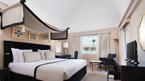 Quarto de hotel com uma cama grande, uma escrivaninha, uma cadeira, uma televisão e uma janela vista para a piscina.
