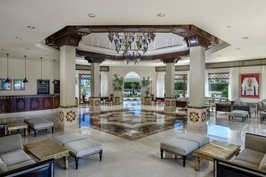 Um hall amplo com piso de mármore central, áreas de estar e um candelabro.