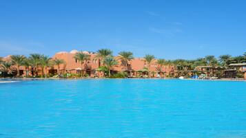 Um resort com uma piscina grande, palmeiras e edifícios em estilo mediterrâneo.