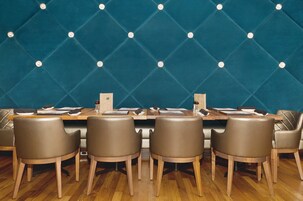 Uma sala de conferências com uma mesa de madeira, seis cadeiras marrons e uma parede acolchoada azul com luminárias circulares.