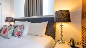 Quarto de hotel com cama, almofadas, abajur e telefone.