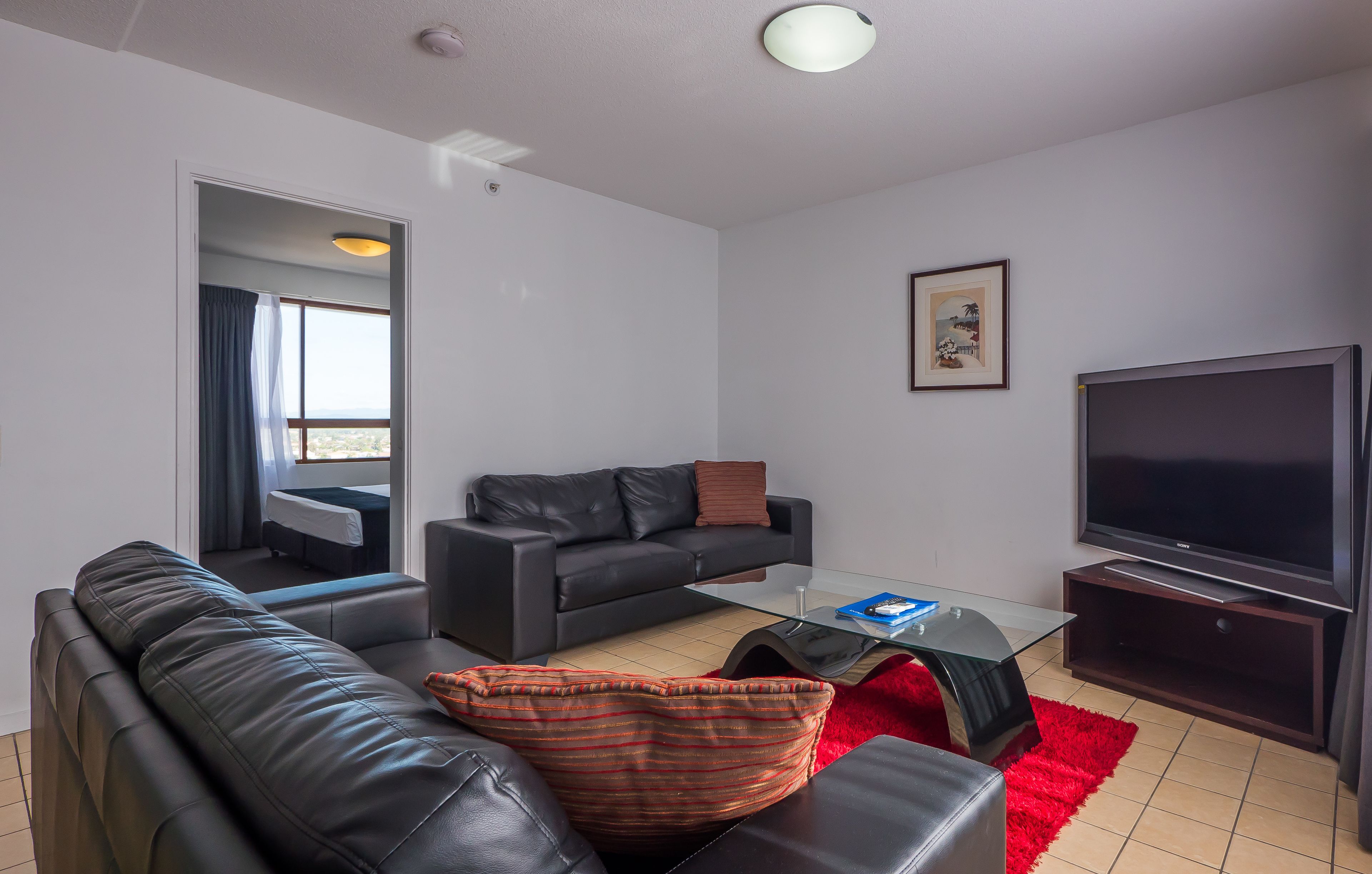 Uma sala de estar moderna com um sofá de couro preto, uma mesa de centro de vidro e uma televisão de tela plana.