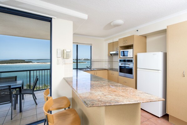 Cozinha moderna com uma ilha grande, micro-ondas e geladeira. Há uma varanda com vista para o mar.