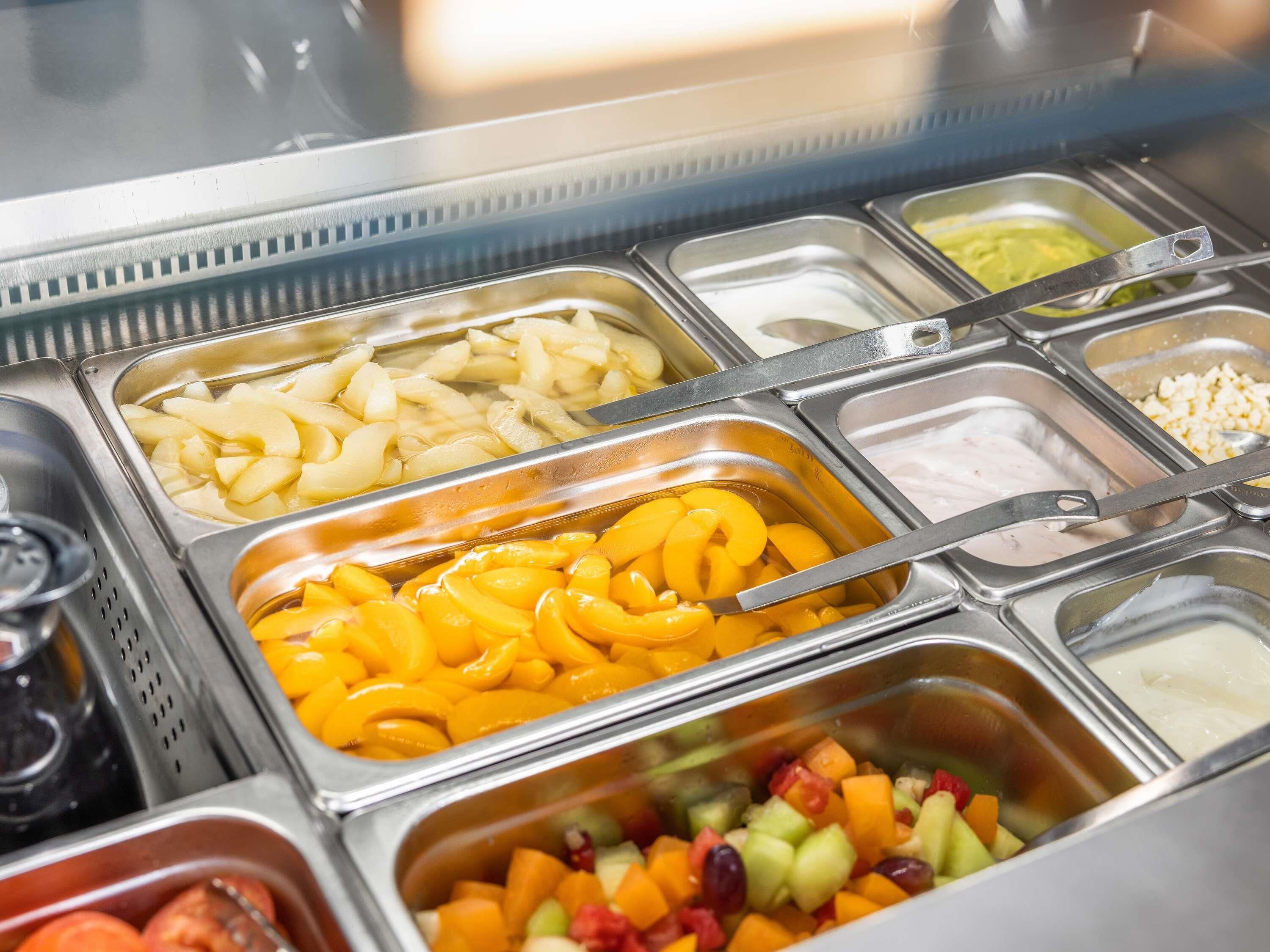 Buffet com diversas opções de comida, incluindo frutas, vegetais e uma salada.