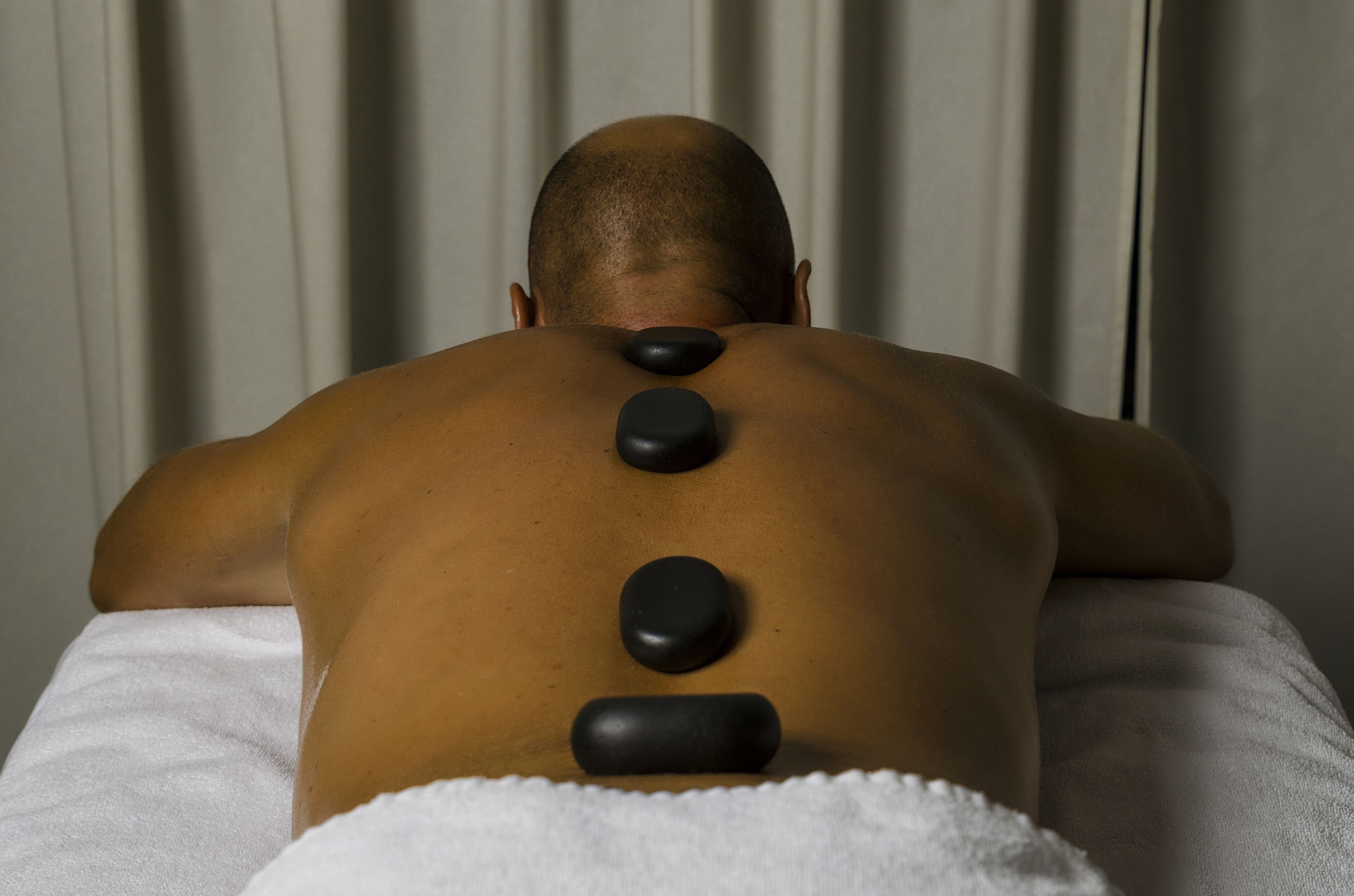 Uma pessoa recebendo massagem nas costas, com três pedras pretas colocadas sobre elas.