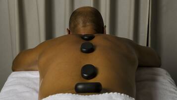 Uma pessoa recebendo massagem nas costas, com três pedras pretas colocadas sobre elas.
