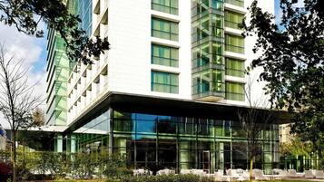 Um hotel moderno com fachada de vidro, área de estar externa e paisagismo bem cuidado.