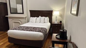 Quarto de hotel bem arrumado com cama, mesa de cabeceira, luminária, cadeira e espelho na parede.