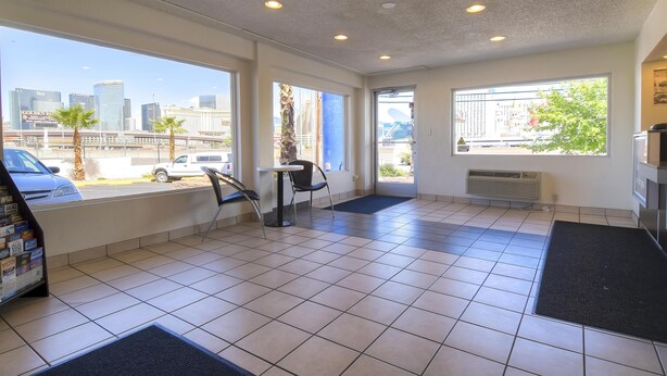 Um espaço interno amplo, com grandes janelas, piso em azulejos e uma área de estar com cadeiras e uma mesa.