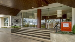 Entrada de um edifício moderno com fachada de vidro, uma coluna de madeira imponente e uma placa.