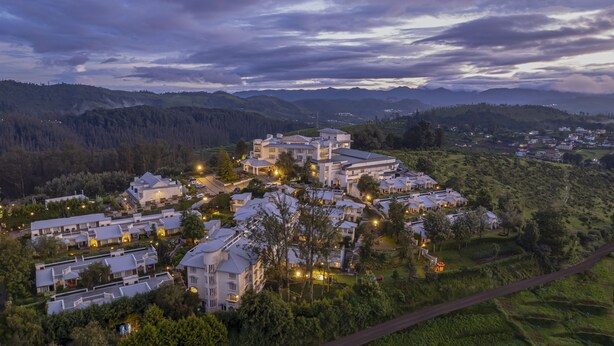 Vista aérea de uma área residencial com vários edifícios, cercada por vegetação e colinas.