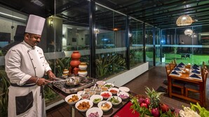 Um chef prepara alimentos em uma cozinha moderna com grandes janelas com vista para um jardim.