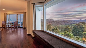 Quarto com uma grande janela que oferece vista para um vale arborizado e montanhas ao longe.
