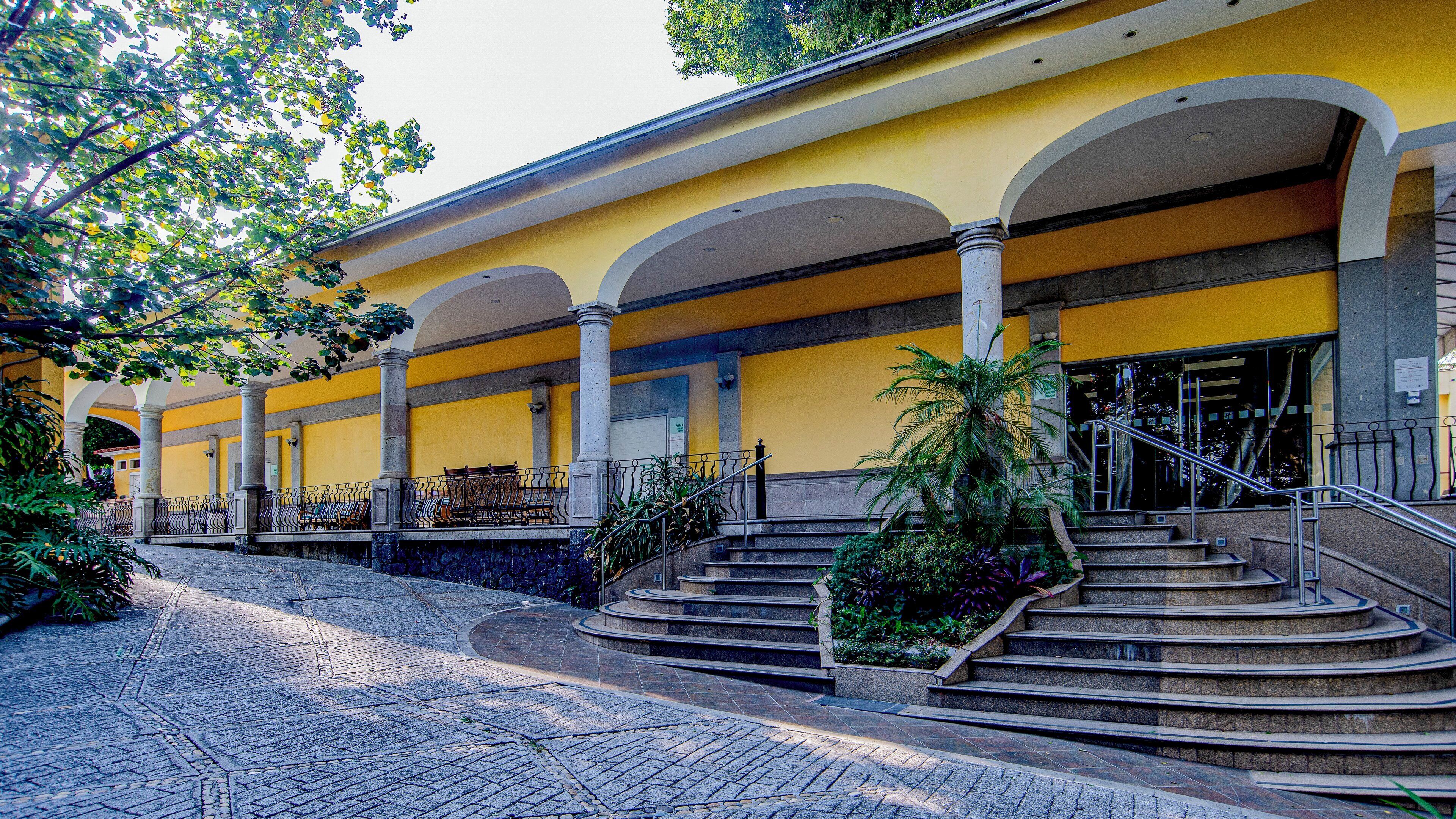 Um edifício com fachada amarela, várias arcadas e uma escadaria que leva a uma entrada.