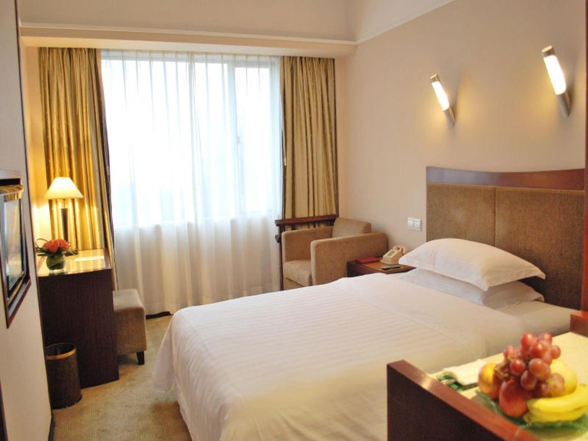 Quarto de hotel com uma cama grande, uma escrivaninha com luminária, uma cadeira e uma mesinha de cabeceira com telefone.