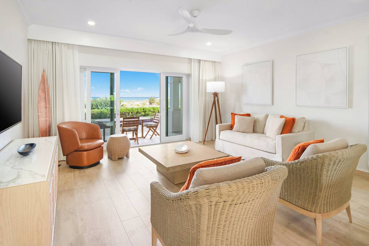Uma sala de estar moderna com sofá, cadeiras, mesa de centro, TV e uma varanda com vista.